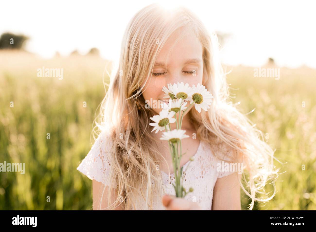 Blond girl smelling fresh flowers in field Stock Photo - Alamy