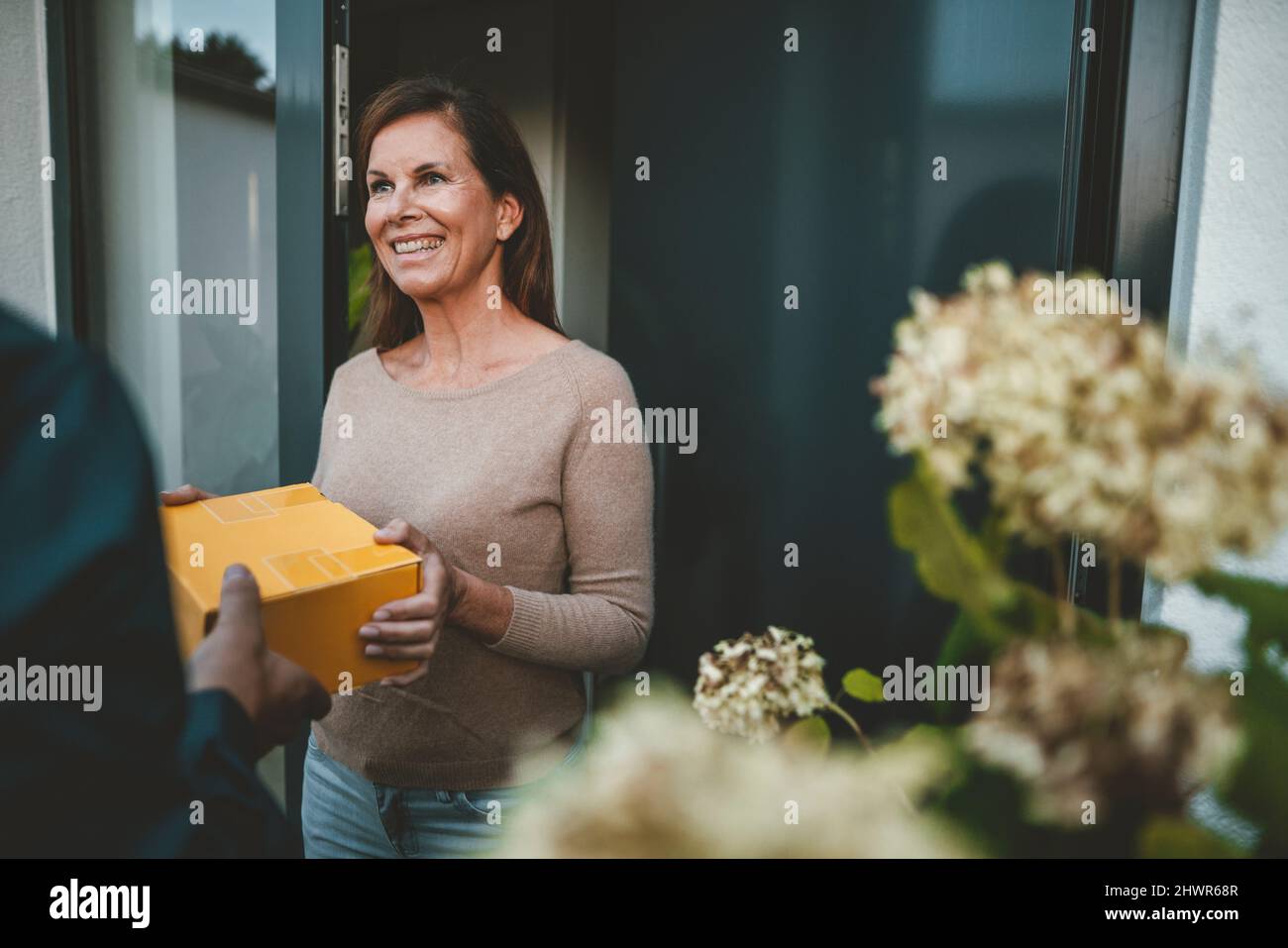 Happy woman receiving yellow package from delivery person at doorway ...