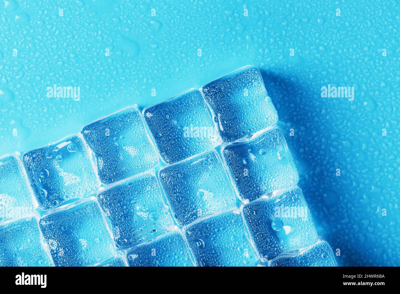 Ice cubes with water drops scattered on a blue background, top view ...