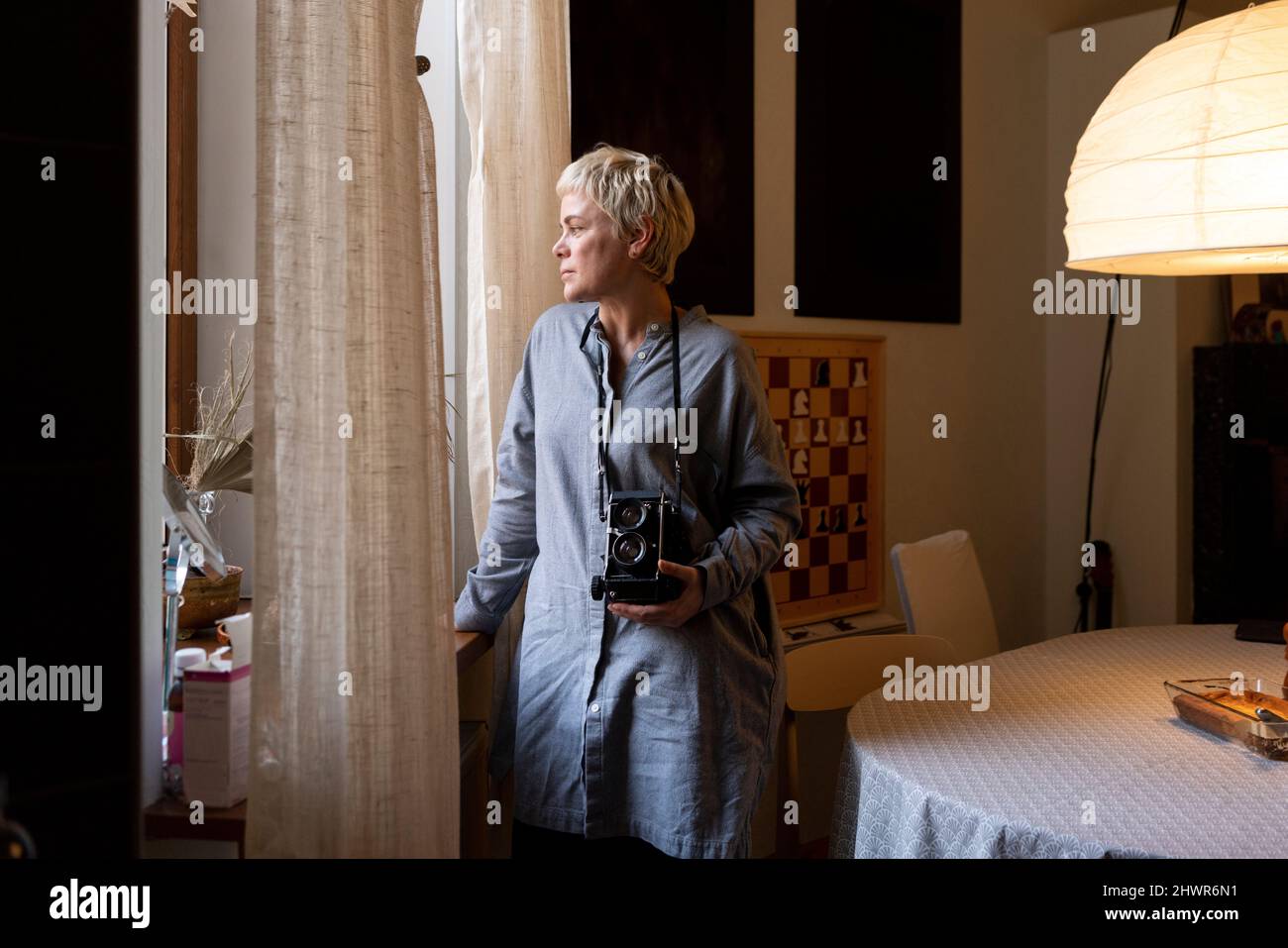 Photographer with camera looking through window at home Stock Photo - Alamy