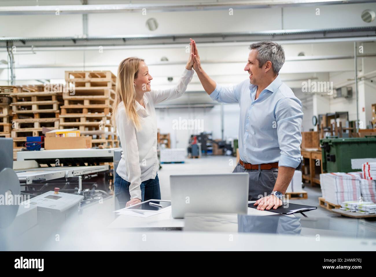 Happy businessman and businesswoman giving high-five at factory Stock ...