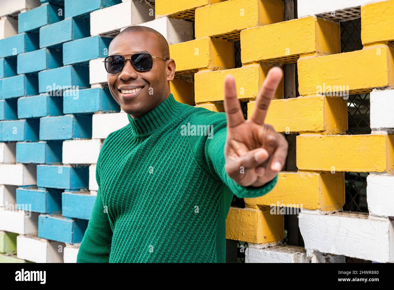 Happy man gesturing peace sign in front of brick wall Stock Photo - Alamy