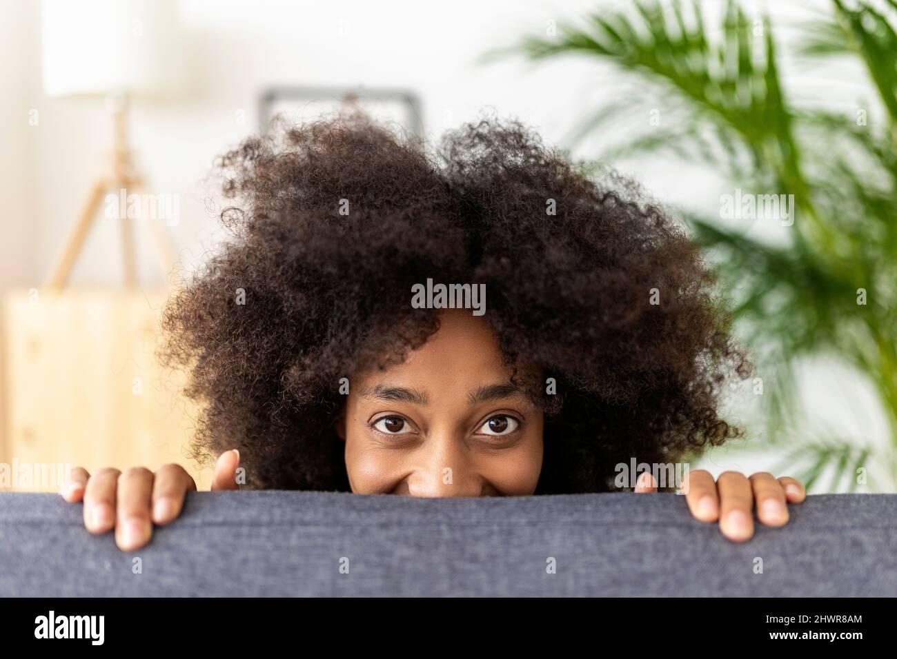 Young woman peeking behind sofa in living room at home Stock Photo - Alamy