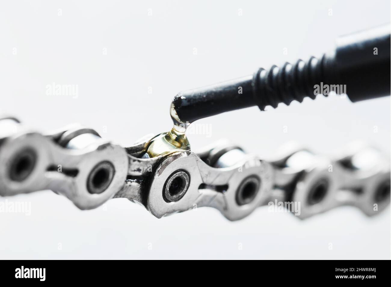Greasing a bicycle chain with a drop of golden oil close-up on a gray ...