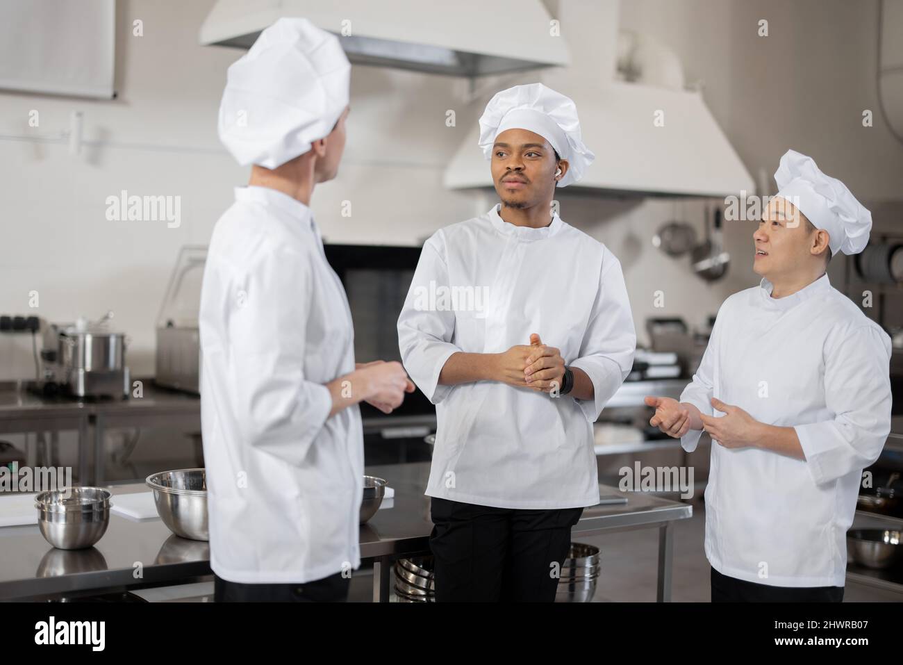 Three multiracial chef cooks talk while standing together during a ...
