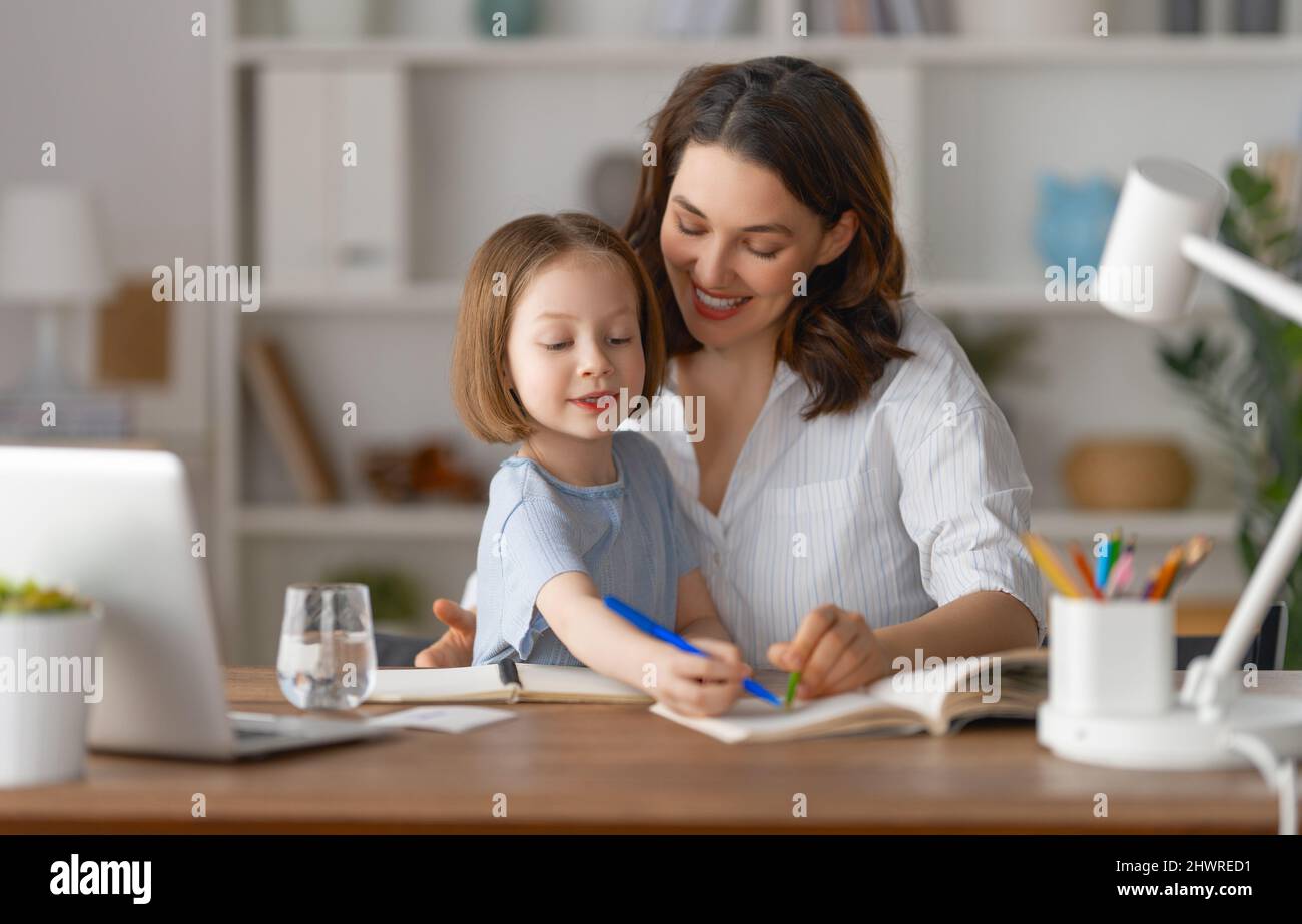 Happy child and adult are sitting at desk. Girl doing homework or ...