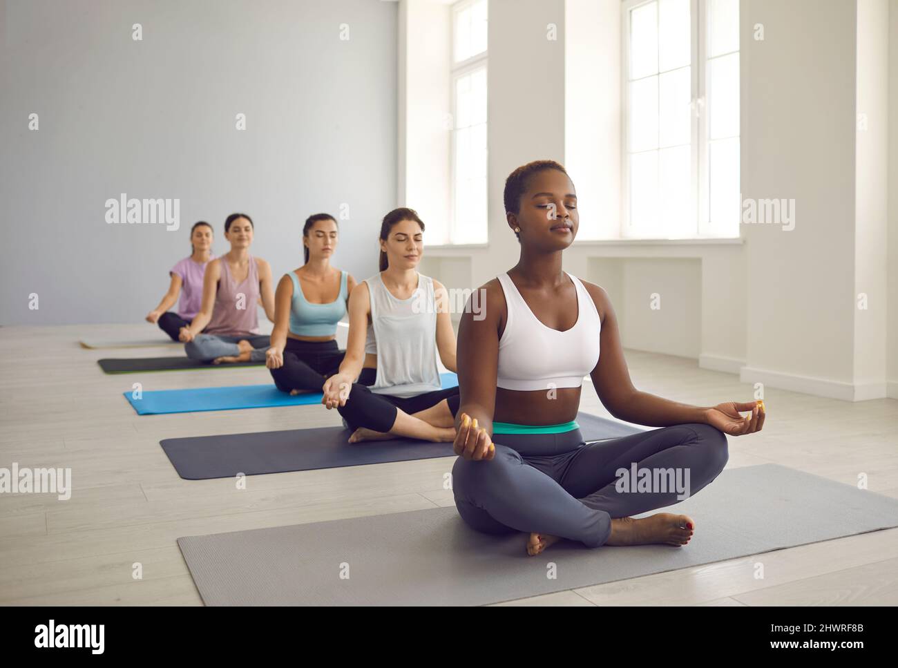 Group of relaxed young women enjoying meditation in lotus pose at gym ...