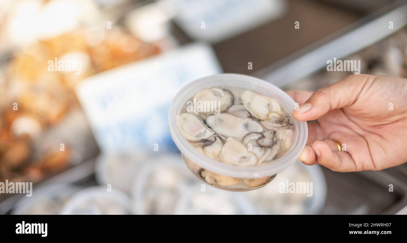 Female customers choosing fresh raw shellfish seafoods in plastic box ...