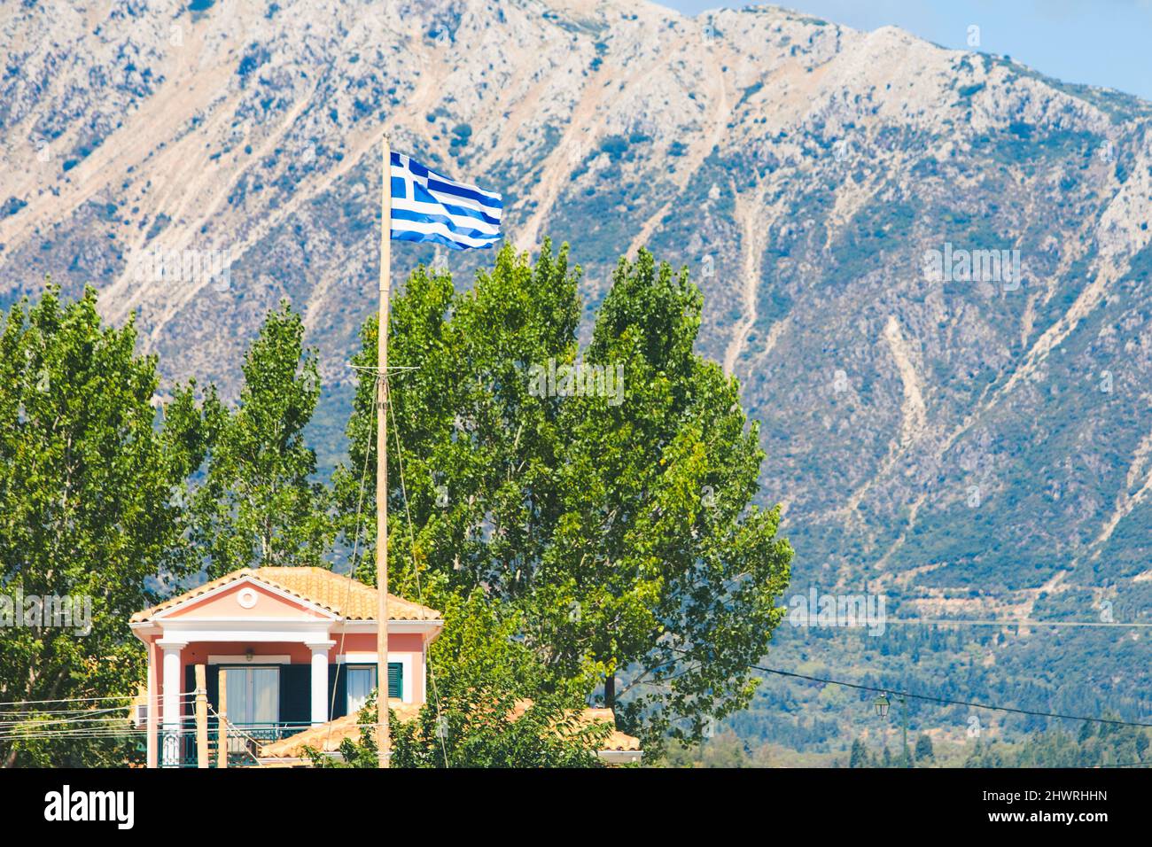 The Greek flag is flying on the flagpole on a sunny day. mountains in ...