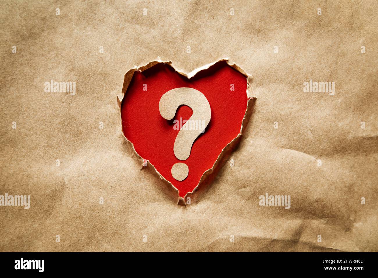 Heart shaped hole in kraft paper. Inside a question mark on a red ...