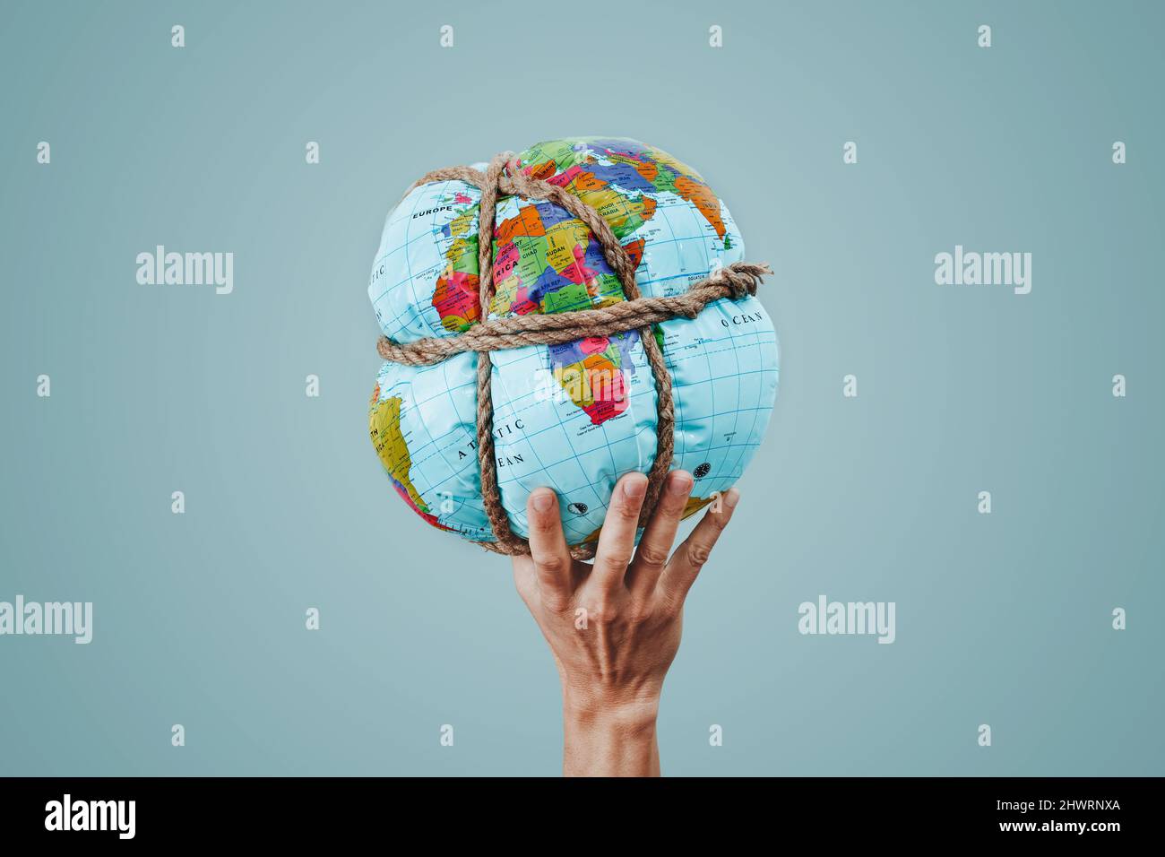 a young man holds an earth globe tightly tied with rope in his hand, on ...