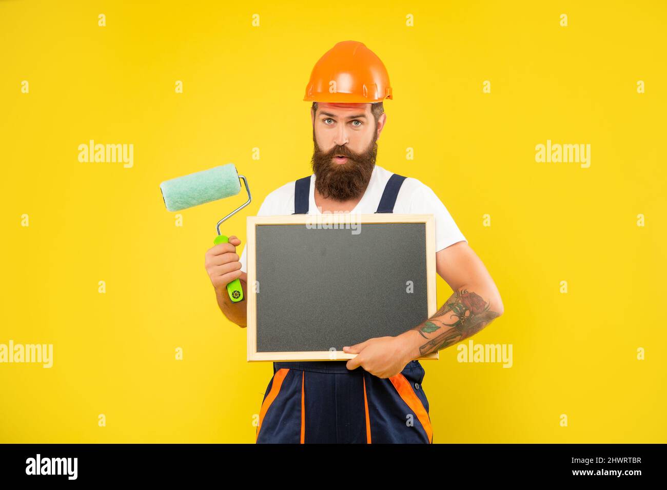 amazed man painter in helmet and work clothes hold paint roller and ...
