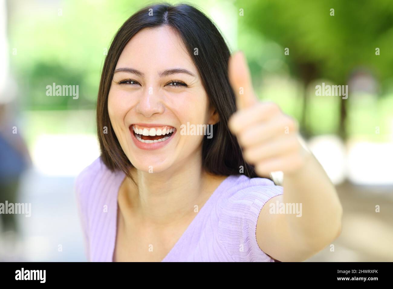 Front view portrait of a happy asian woman gesturing thumb up in a park ...