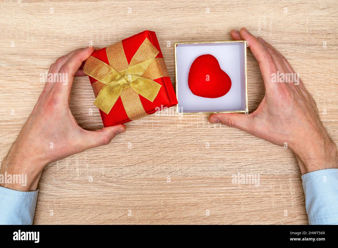 Hands opening a gift box with a tiny red heart inside. Surprise love ...