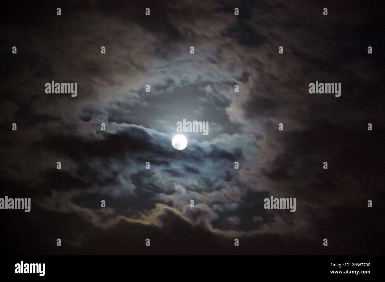 Full moon shining glowing light through the darkness of cloudy night ...