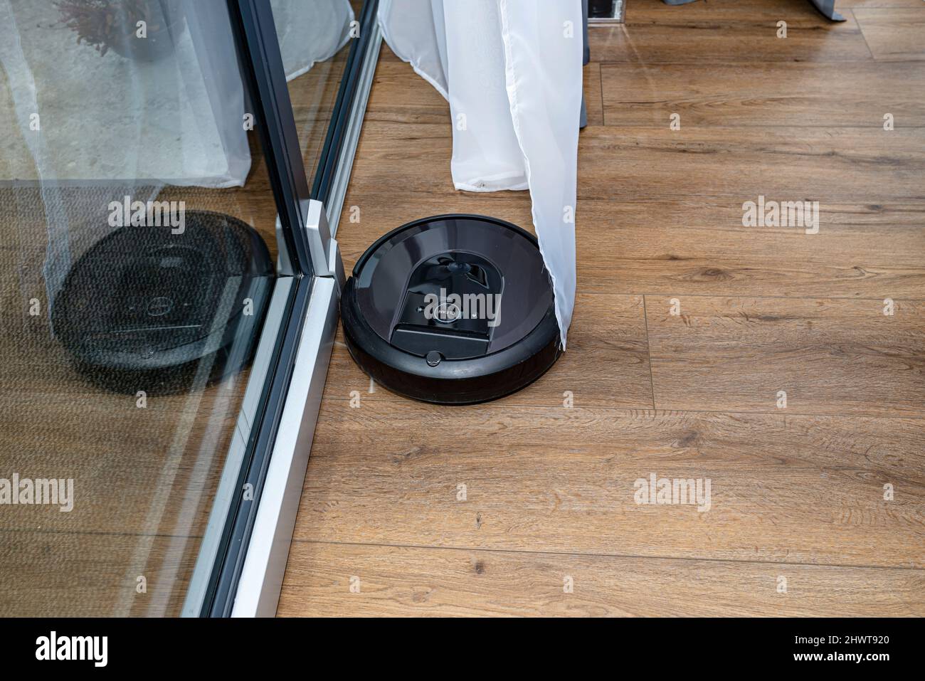 A modern robotic vacuum cleaner cleans vinyl panels by the patio window ...