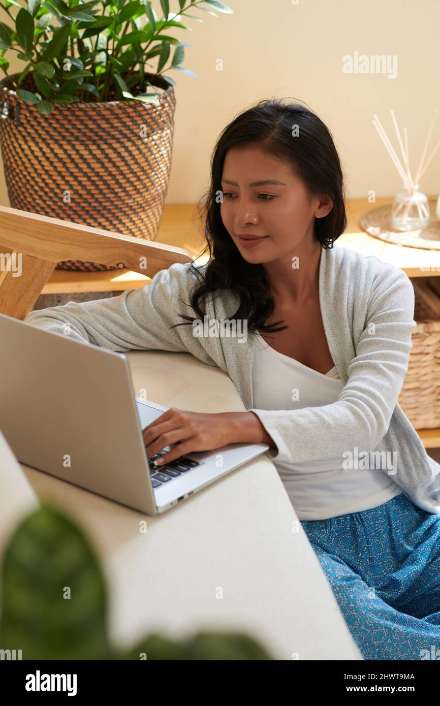 Smiling young woman working on laptop at home, coding or testing new ...