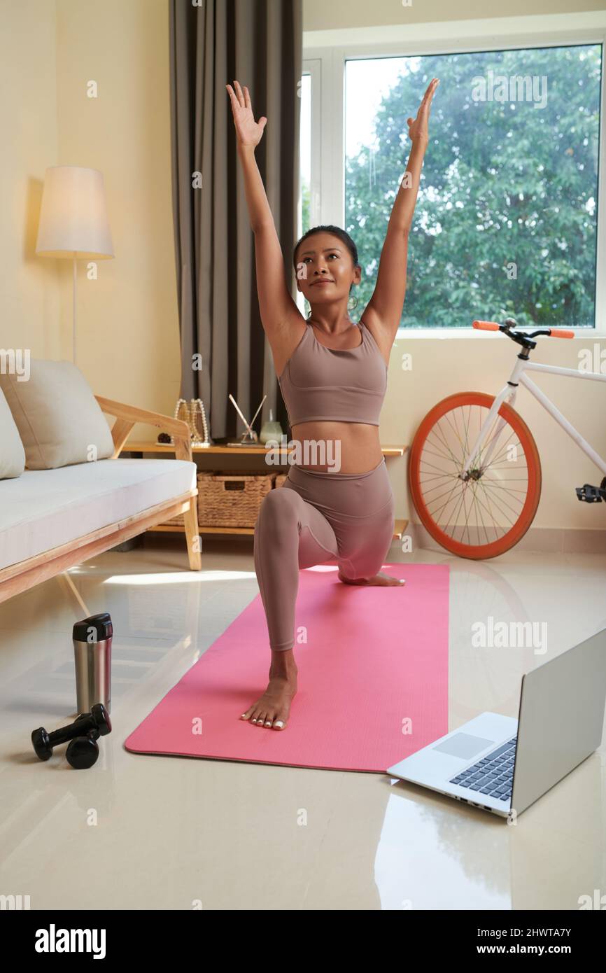 Fit smiling young woman raising arms when doing deep lunges on yoga mat at home Stock Photo - Alamy