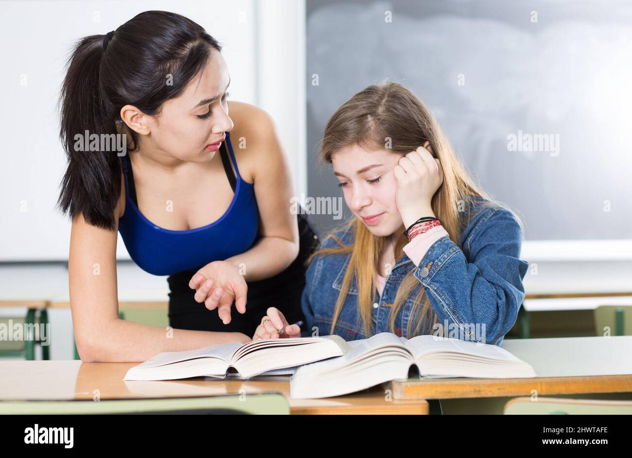 Smiling schoolgirls are learning with help each other at the desk in ...