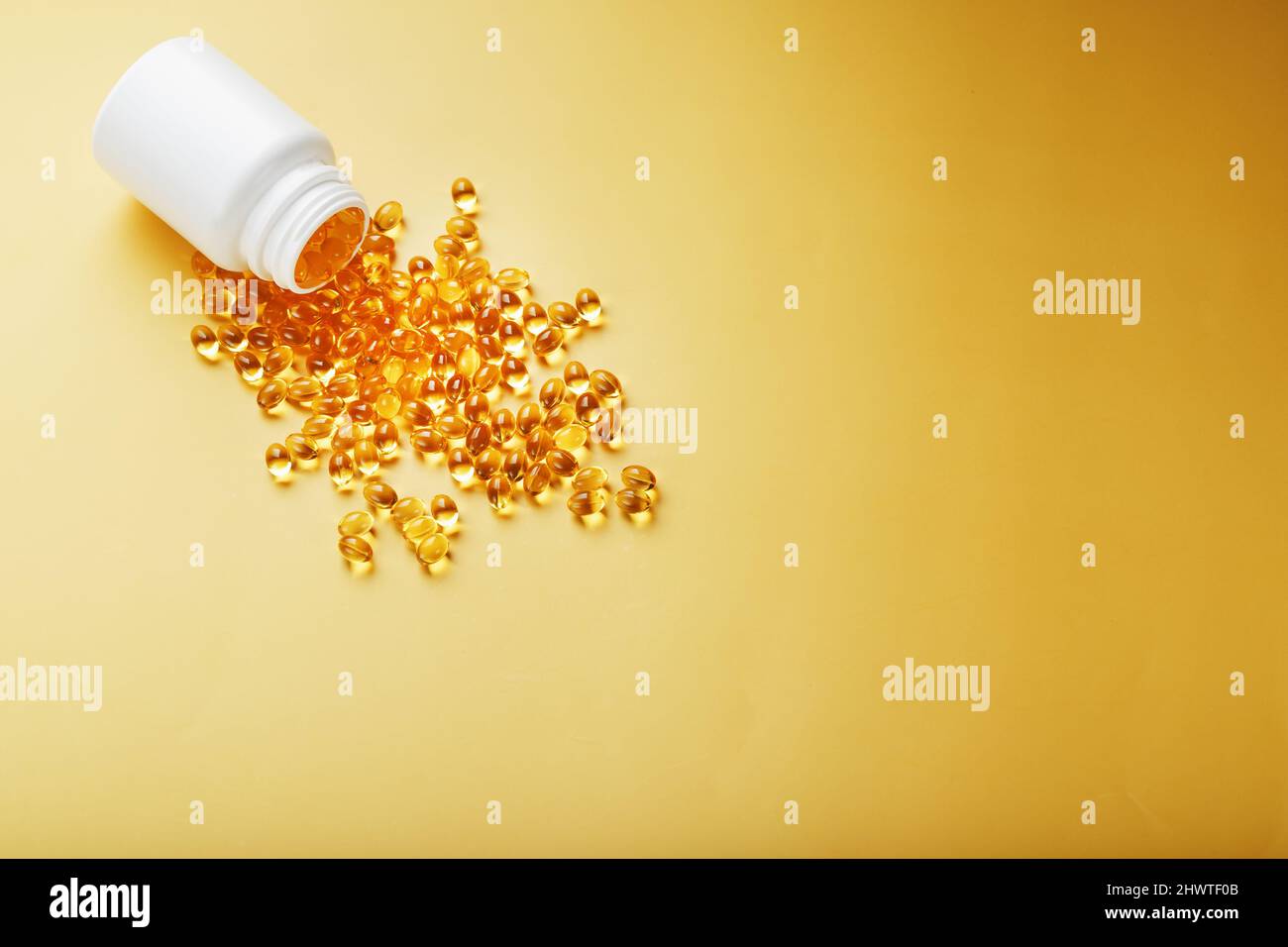 Gold Vitamin D3 capsules poured out of a jar on a yellow background ...