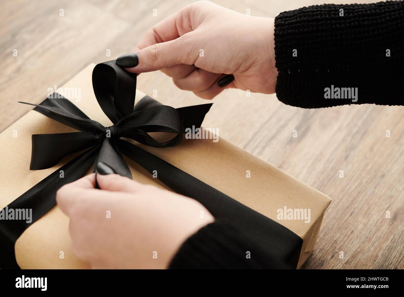 Hands of woman opening birthday present decorated with black ribbon ...