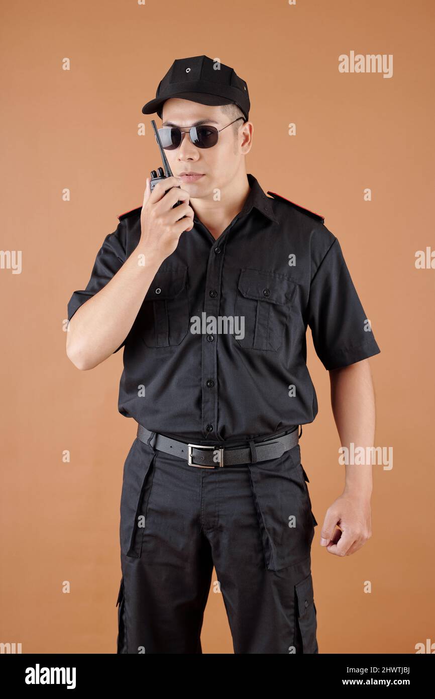 Police officer in black uniform, cap and sunglasses talking in walkie ...