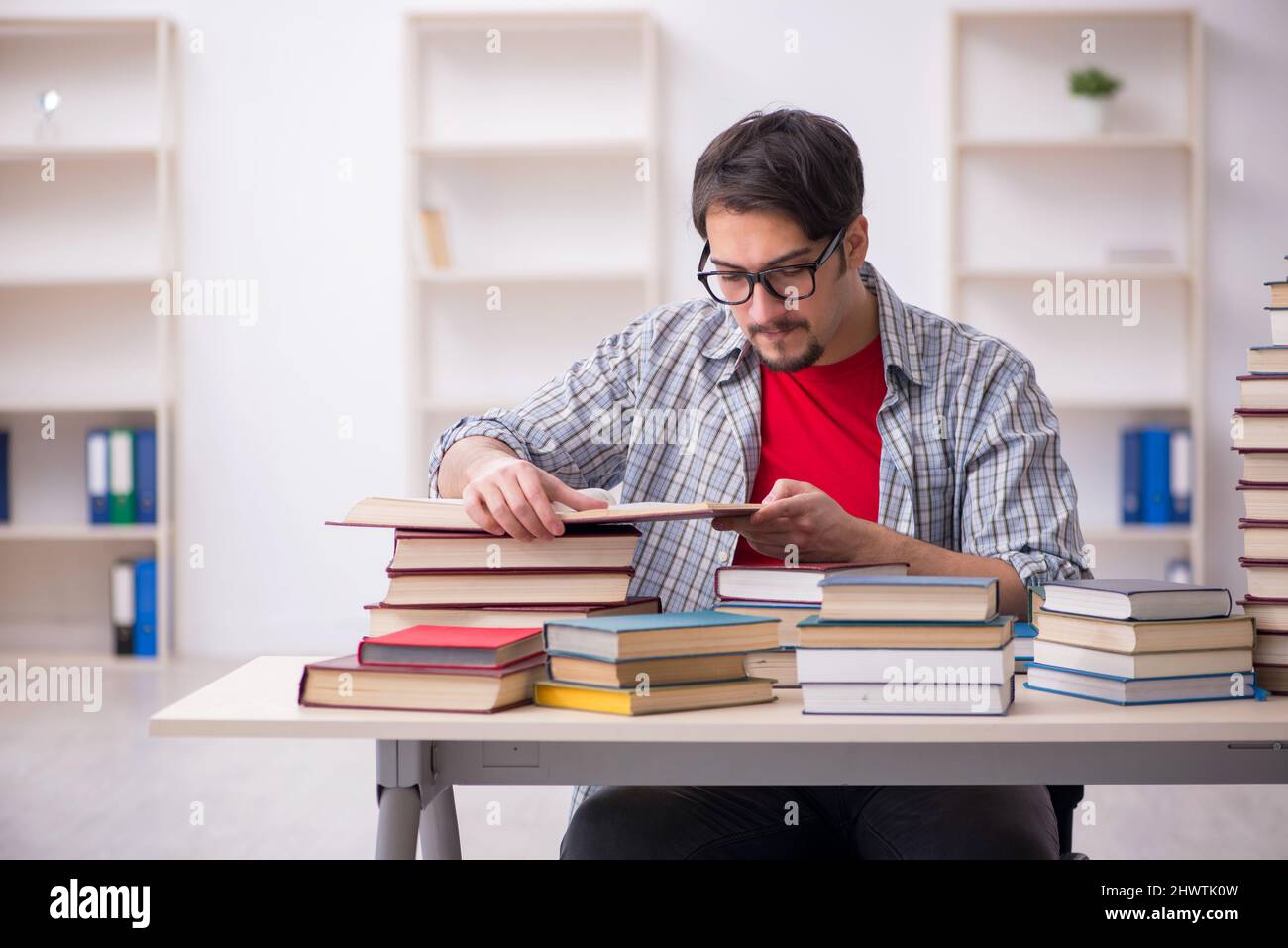 Young student and too many books in the classroom Stock Photo - Alamy