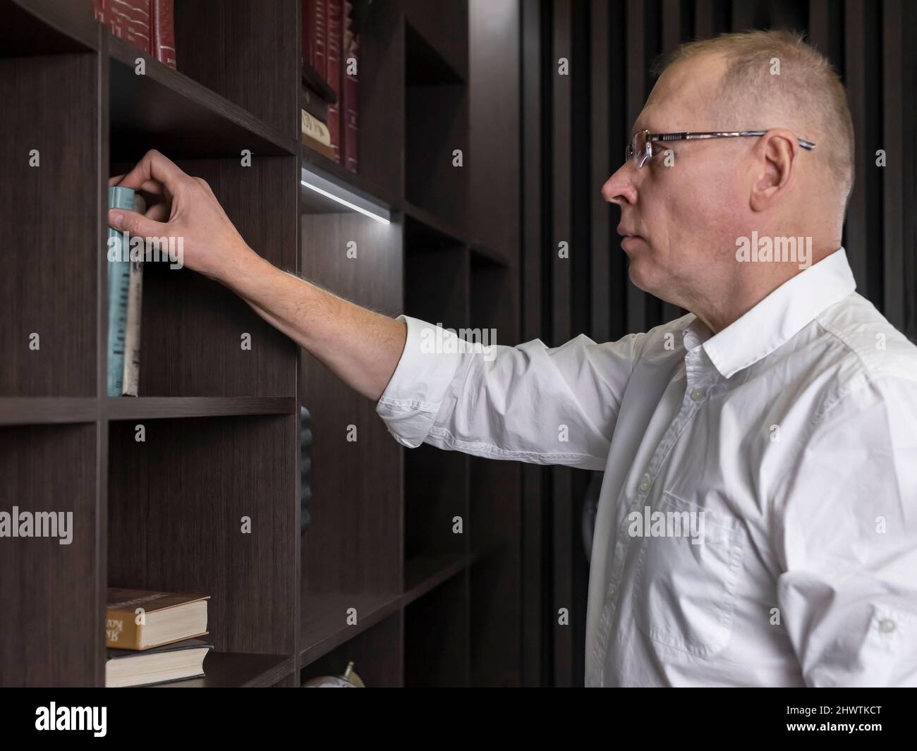 Man taking book from library shelf. Mature businessman going to read ...