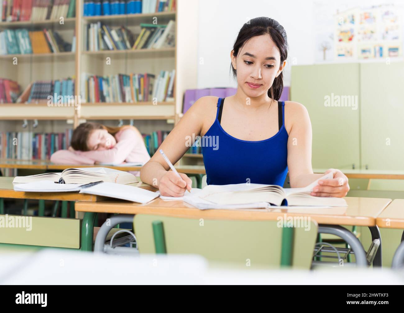 Young girl is sitting at the desk and reading text in the classroom in ...