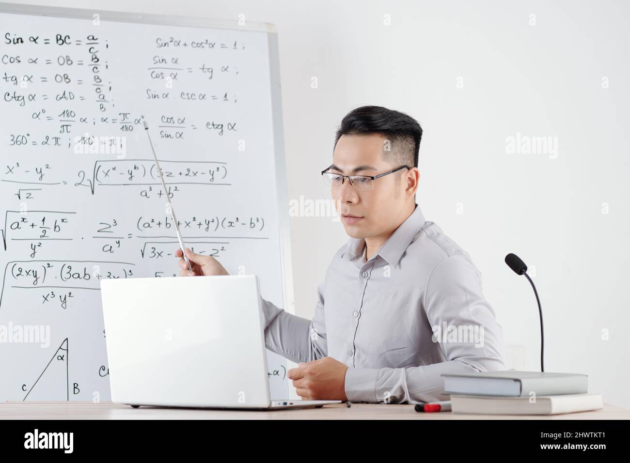 Asian math teacher pointing at whiteboard with formulas when explaining ...