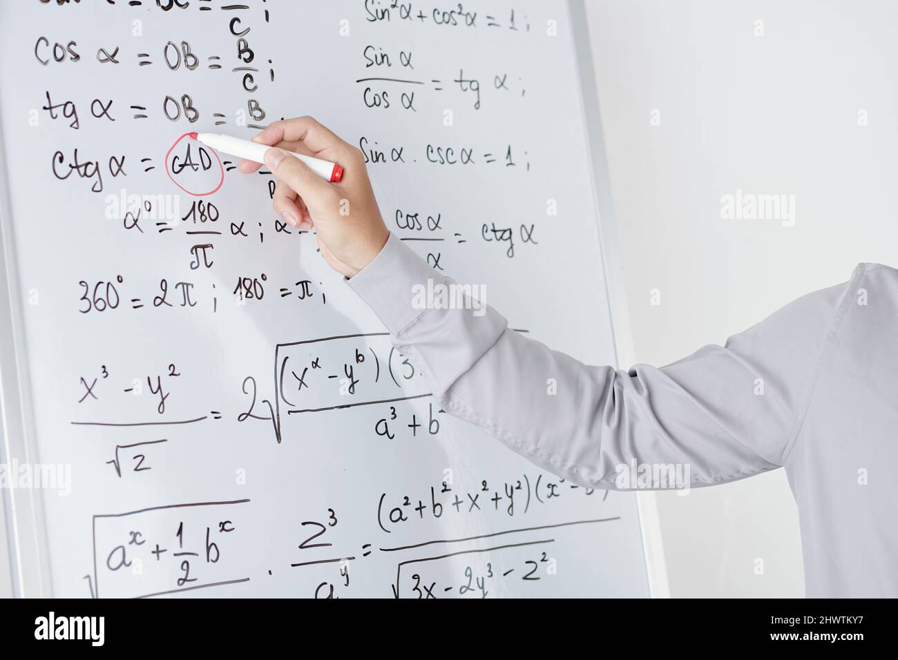 Hands of math teacher circling variable in formula on whiteboard with ...