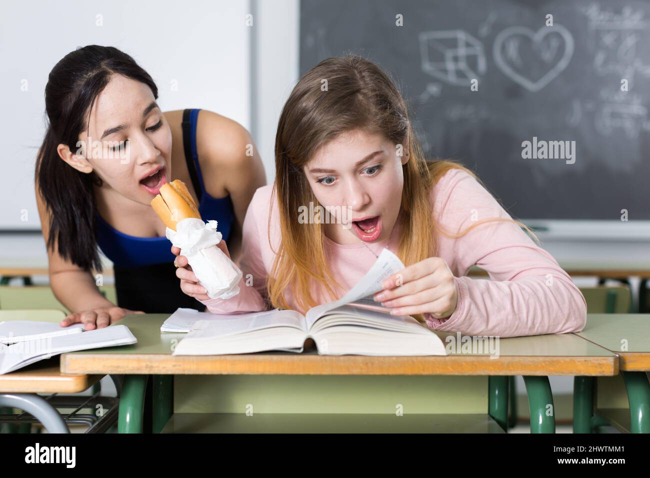 Two girls are eating sandwich at the desk and writing homework in the ...