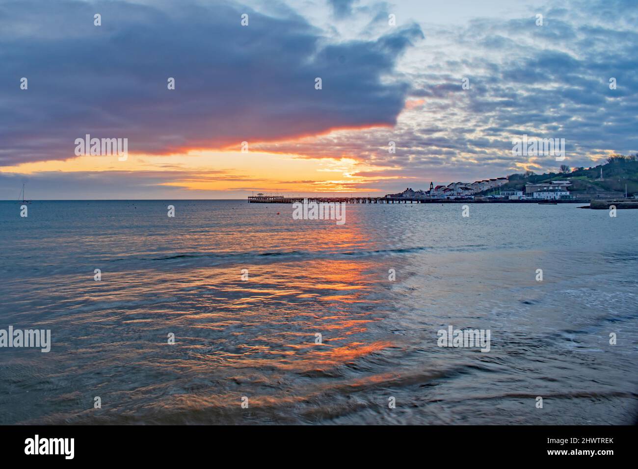 An orange sunrise splits the reflected split sea at Swanage Stock Photo ...