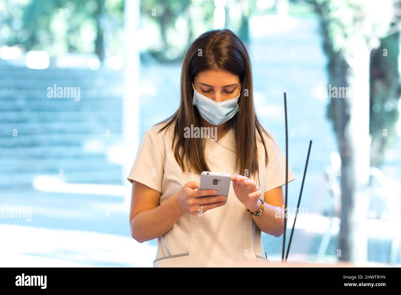 Woman wearing a face mask and using a mobile phone while working in a ...