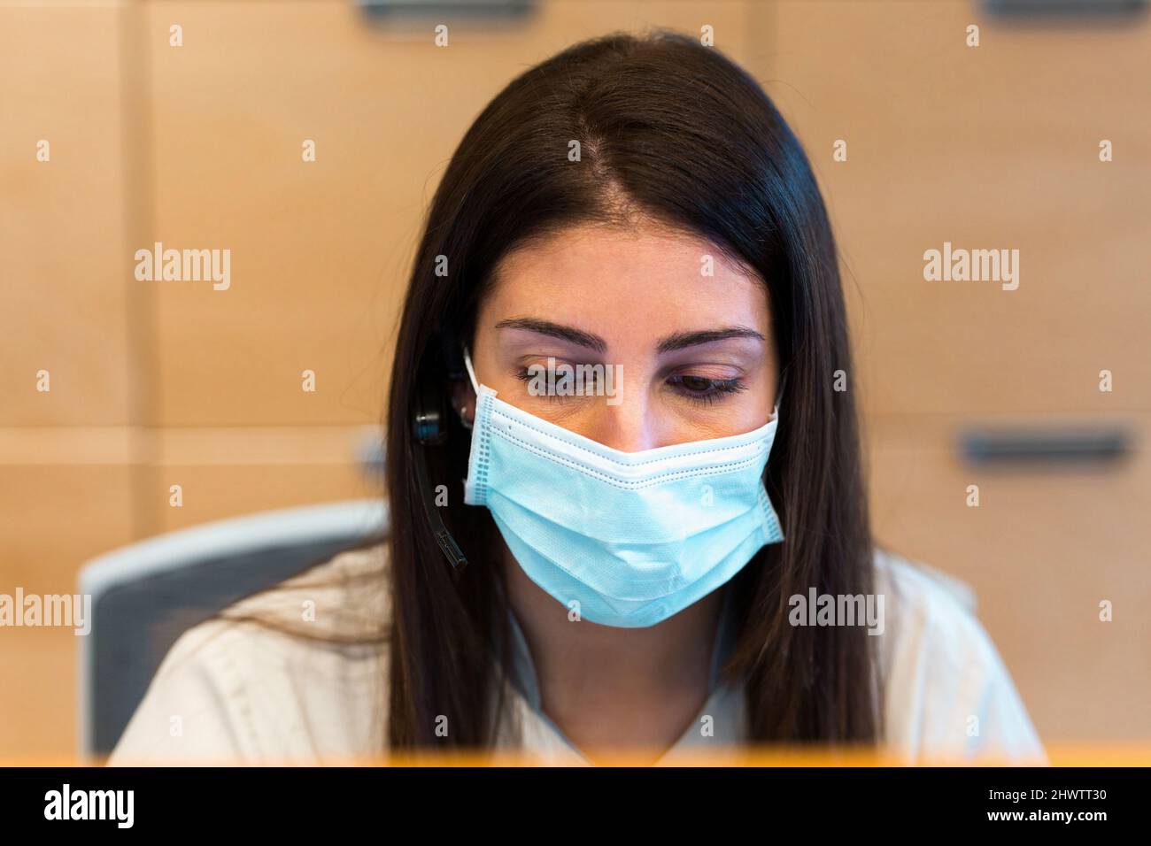 Receptionist wearing surgical face mask sitting at reception while ...