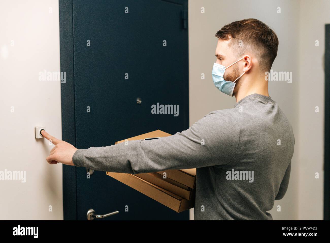 Back view of delivery man in medical mask ringing doorbell of customer ...