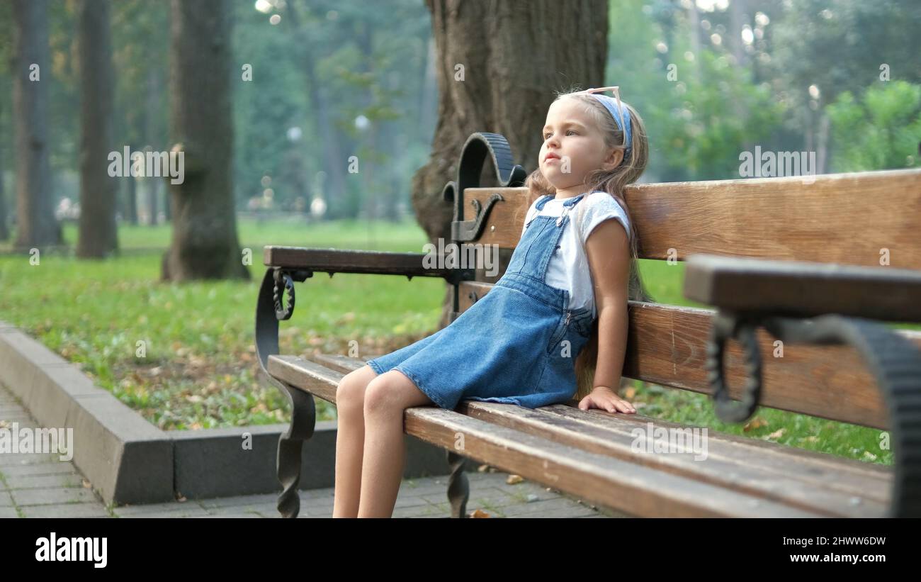 Little child girl sitting alone on a bench in summer park Stock Photo ...