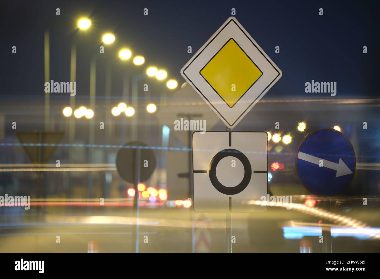 Roundabout road signs with blurred cars on city street traffic at night ...