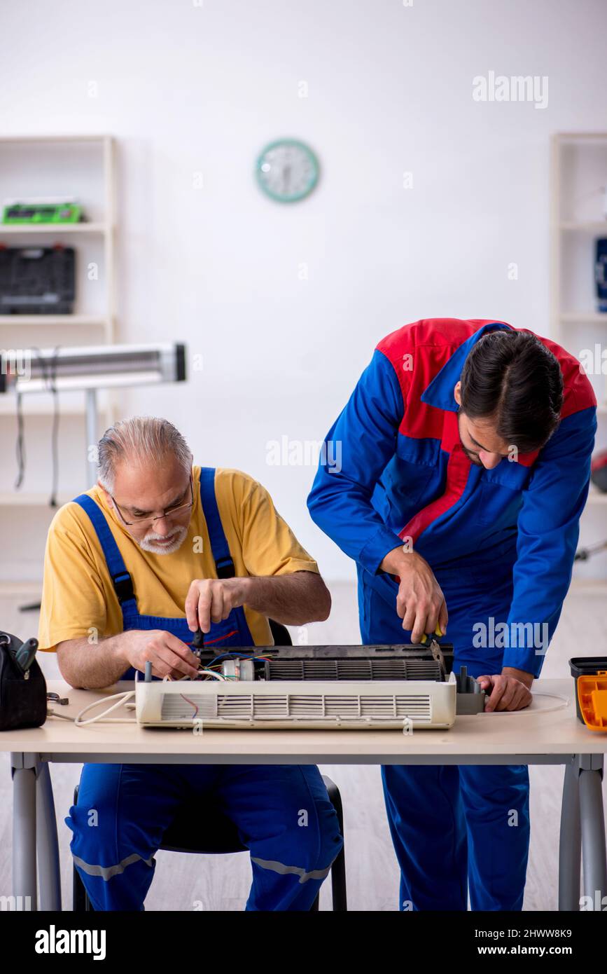 Two repairmen repairing air-conditioner at workshop Stock Photo - Alamy