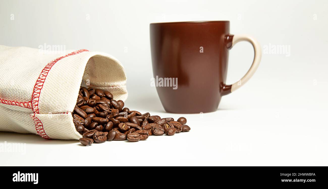 Coffee beans spilled out of the bag on a white background. Brown mug ...