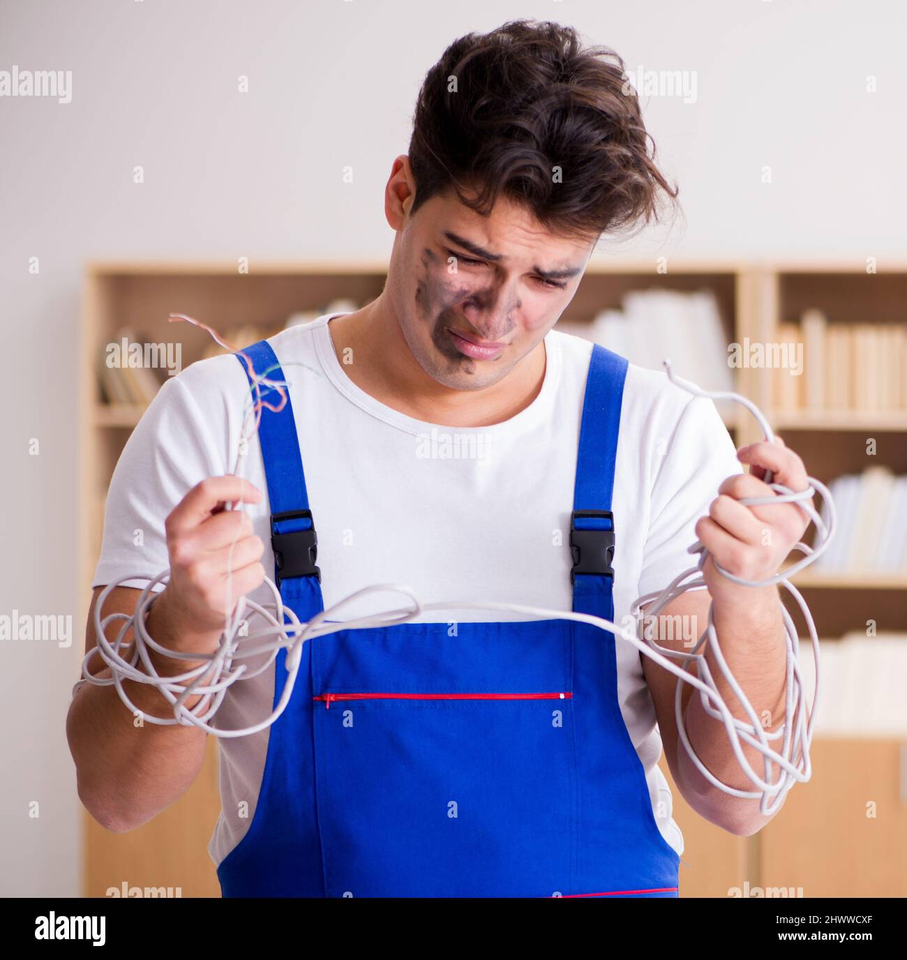 The funny young electrician tangled in cables Stock Photo - Alamy