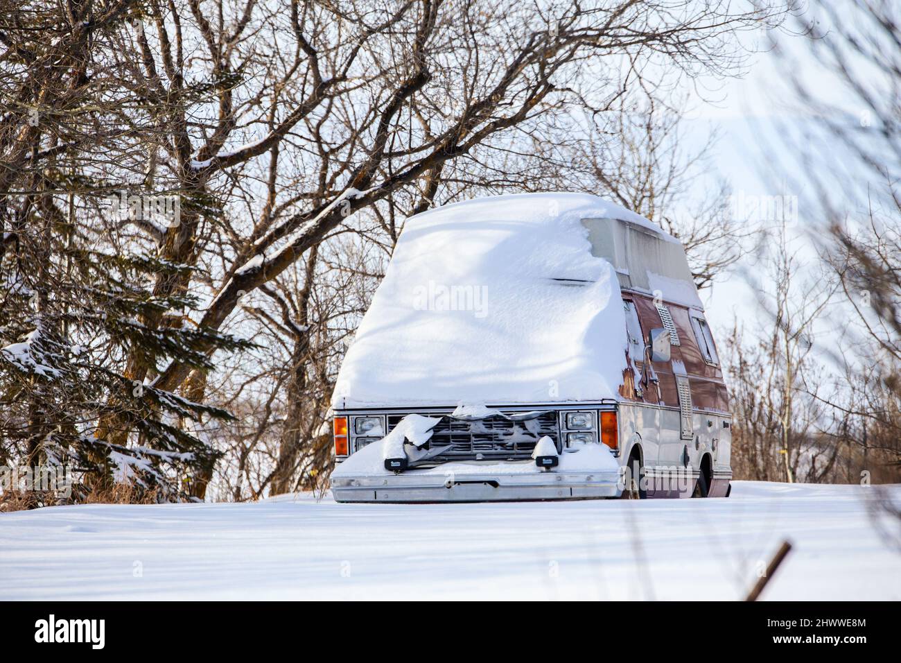 A 1980s style high topper touring bus parked beside trees in a winter ...