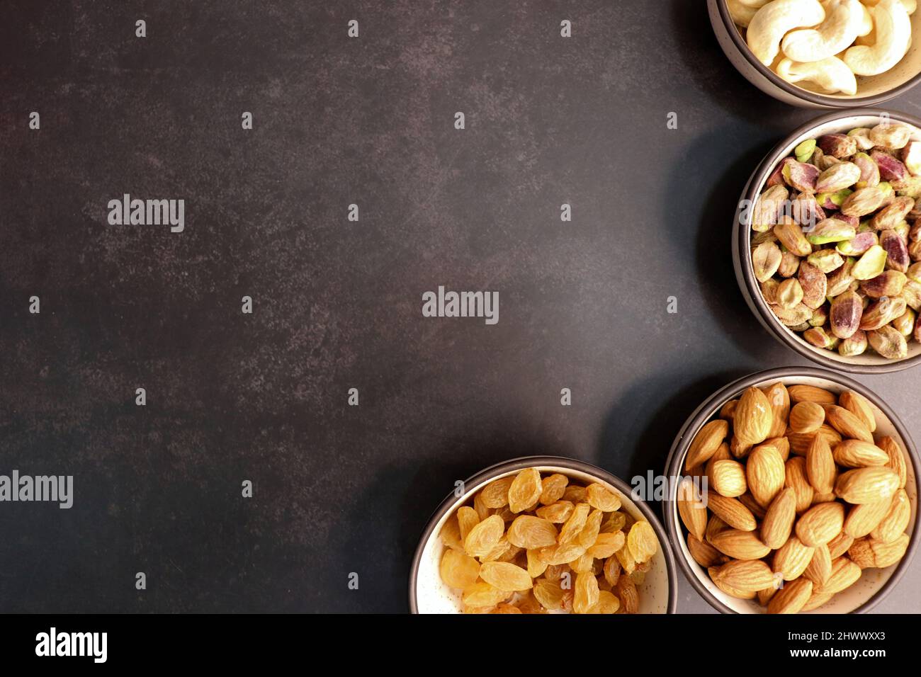 Various varieties of nuts and dried fruits are in a bowls on black ...