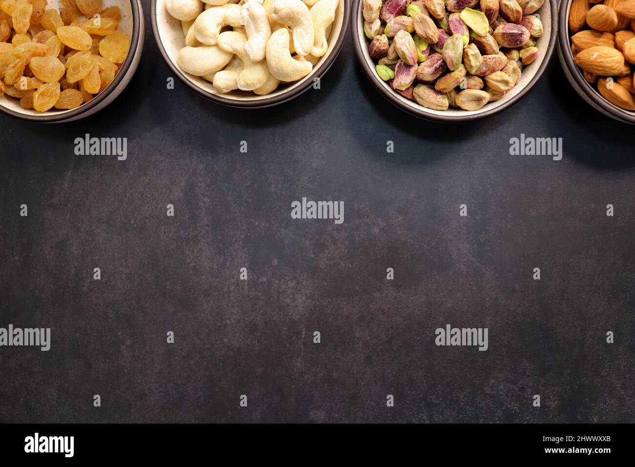 Various varieties of nuts and dried fruits are in a bowls on black ...