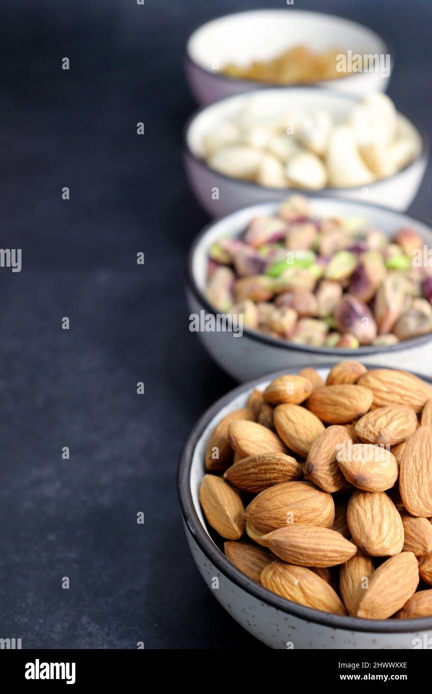 Various varieties of nuts and dried fruits are in a bowls on black ...