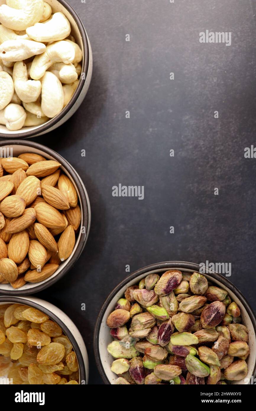 Various varieties of nuts and dried fruits are in a bowls on black ...