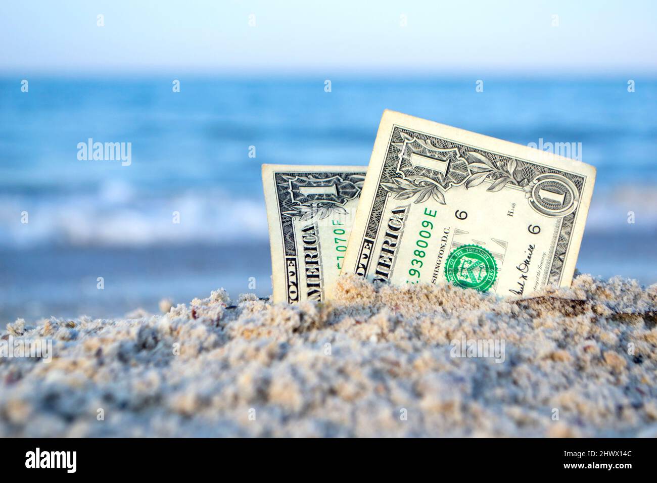 Two one dollar bills half buried in sand on sandy seashore close-up ...
