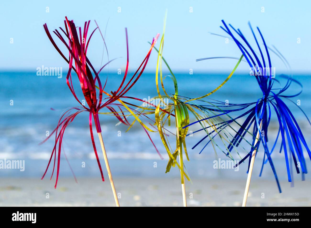 Three bright shiny colored cocktail decorations on stick stand in sand ...