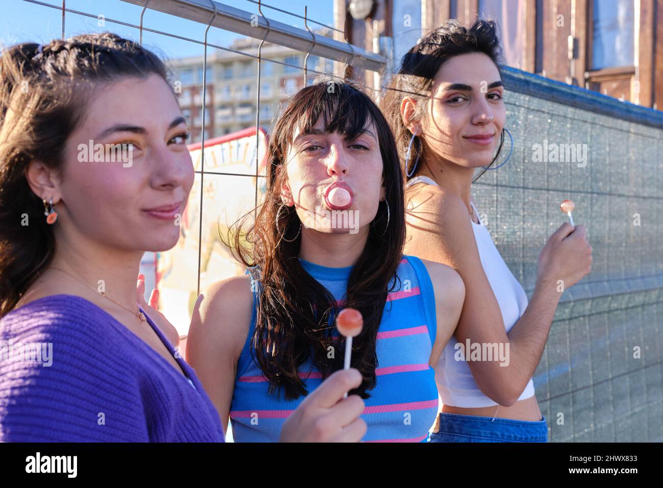 Three young women eating lollipops and blowing bubbles with chewing gum ...