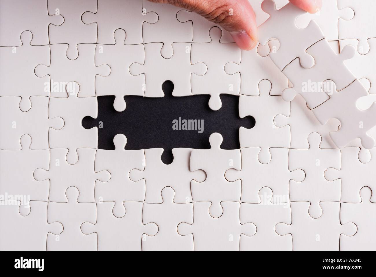 Top view flat lay of hand-holding last piece white paper jigsaw puzzle ...